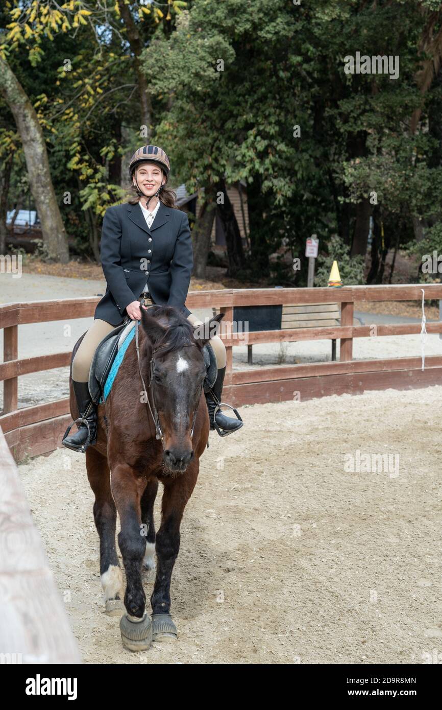 woman riding horse, english saddle, in arena surrounded by oak trees ...