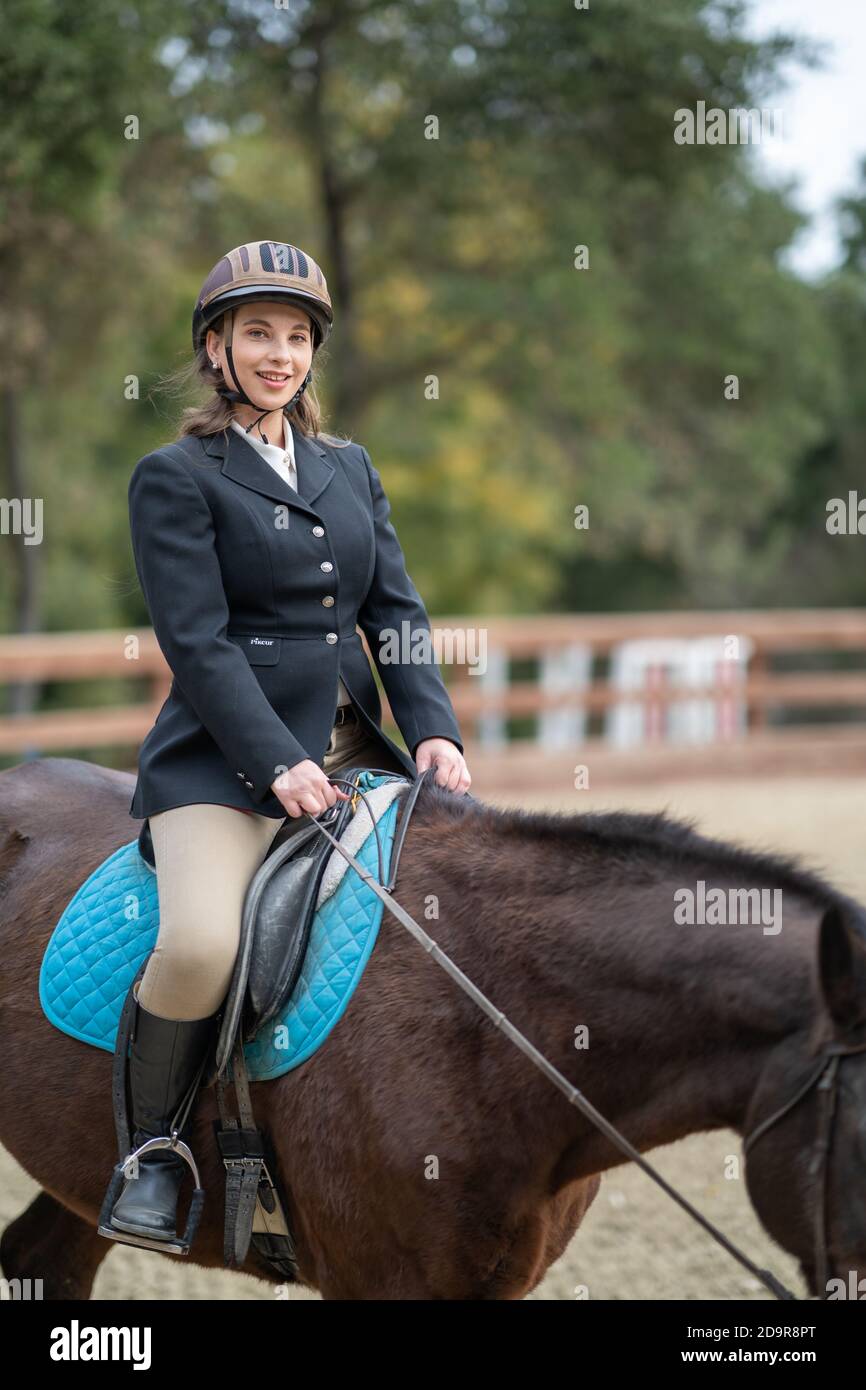 woman riding horse, english saddle, in arena surrounded by oak trees ...