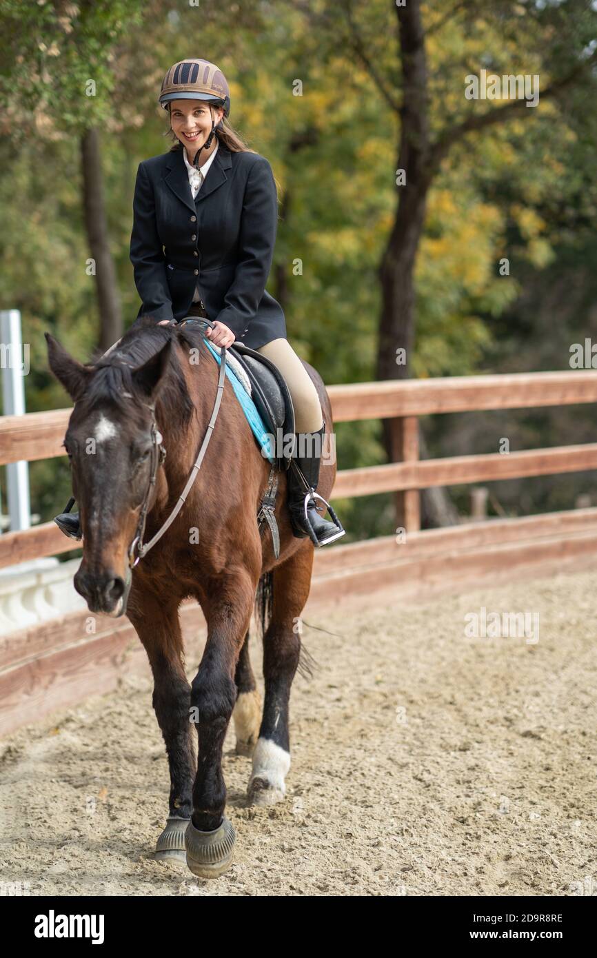 woman riding horse, english saddle, in arena surrounded by oak trees ...