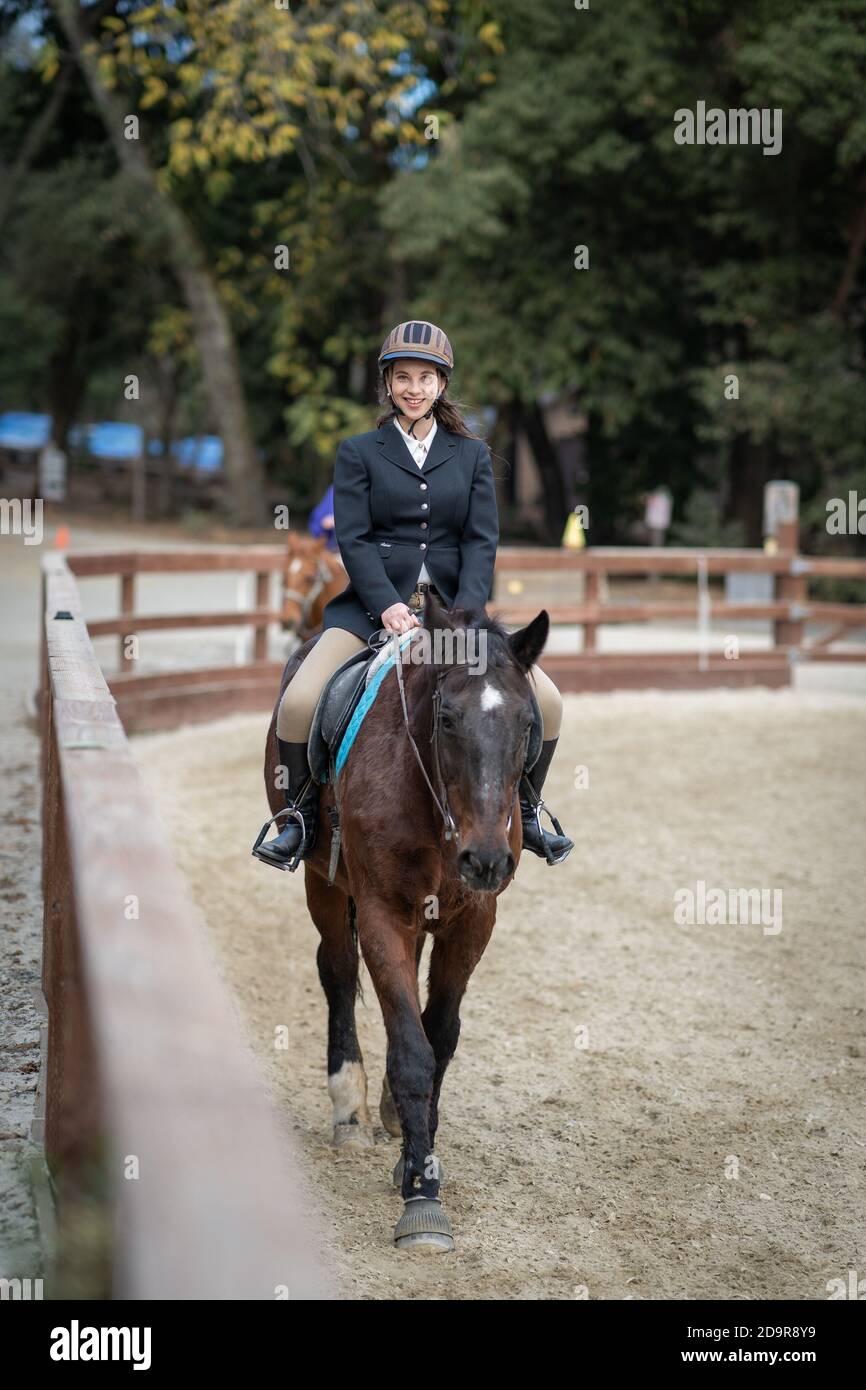 woman riding horse, english saddle, in arena surrounded by oak trees ...