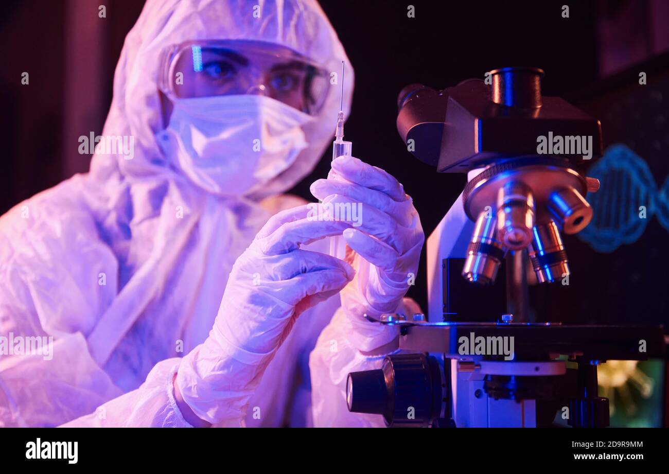 Nurse in mask and white uniform, holding syringe and sitting in neon ...