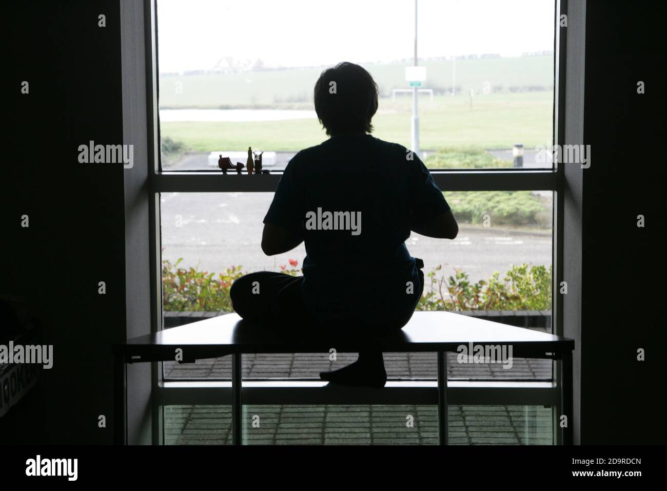 Back view of a autistic child silhouetted looking out of a window , sat ...