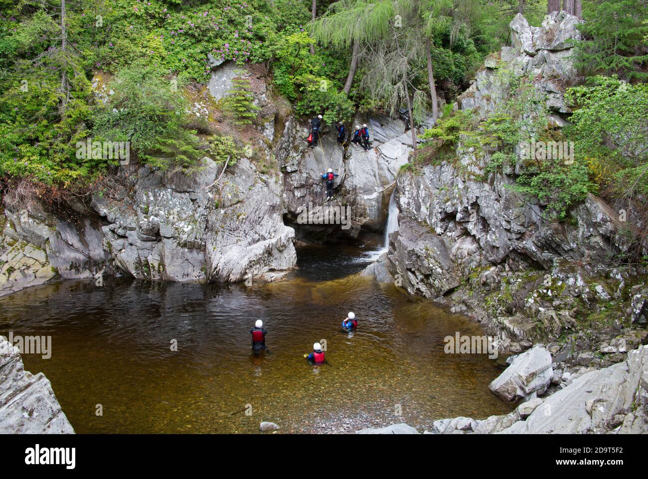 People abseiling down rockface and into a pool under the Falls of Bruar ...