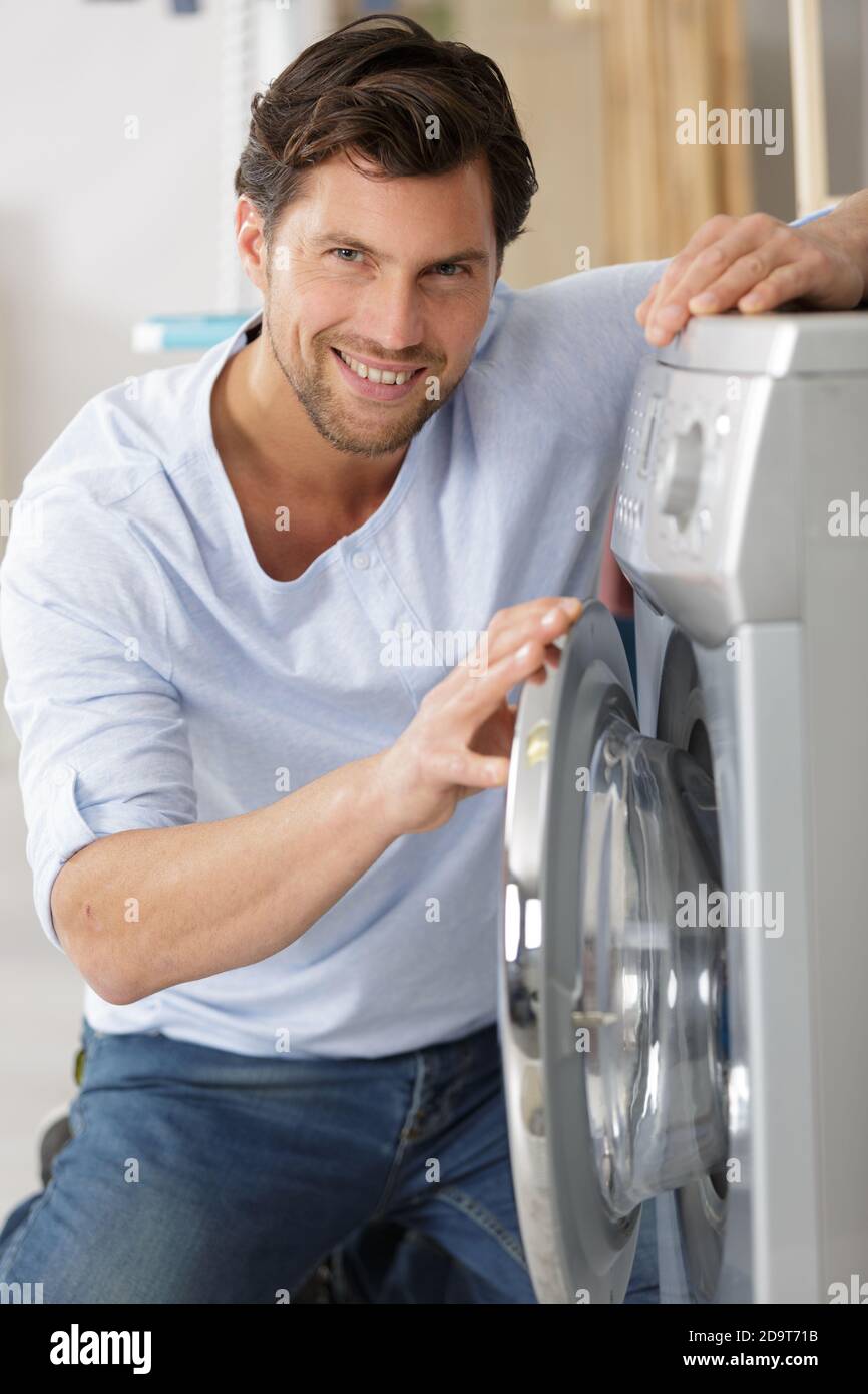 man putting clothes into washing machine and smiling Stock Photo - Alamy