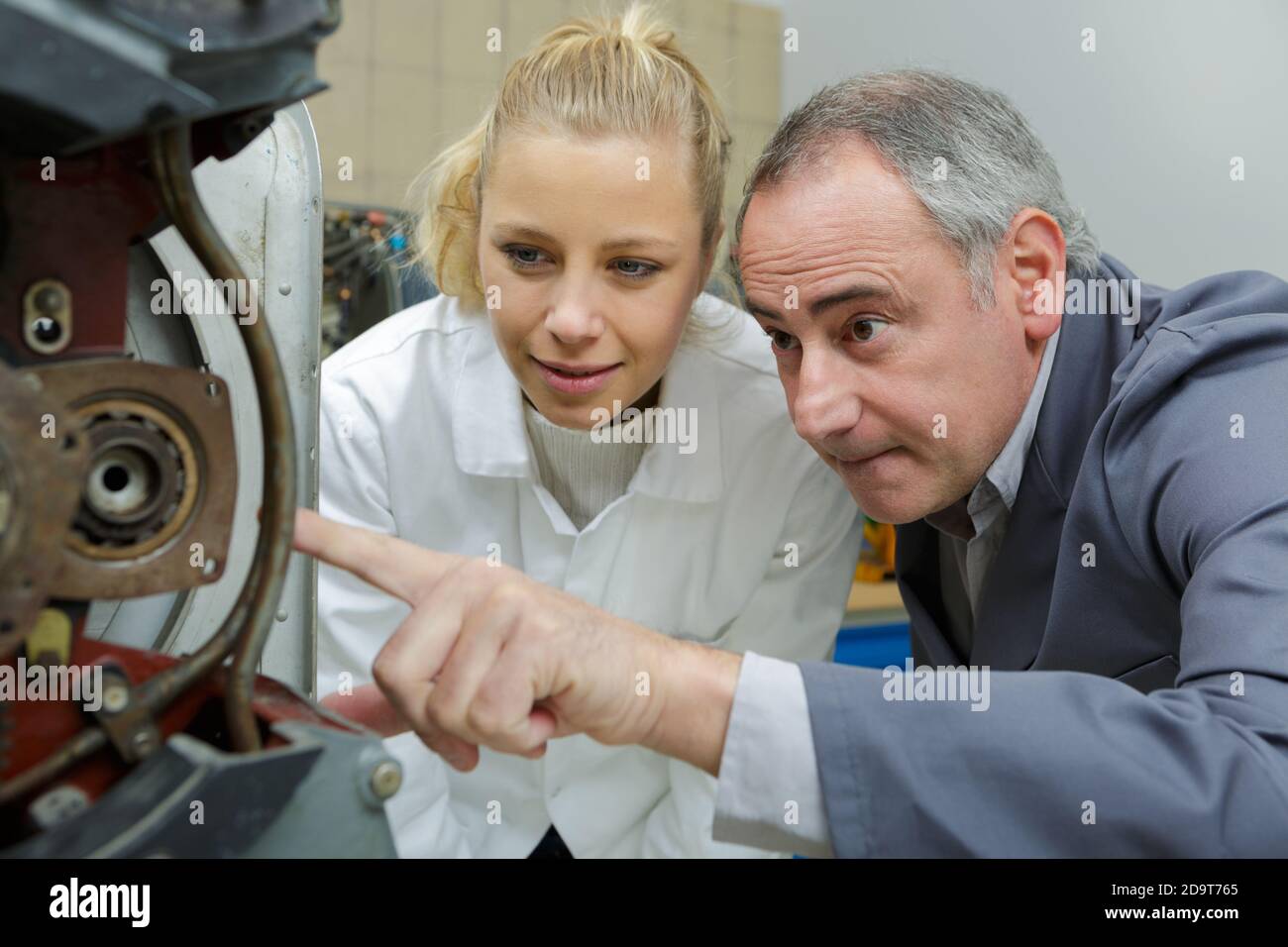 technician explaining working of aircraft part to female apprentice ...