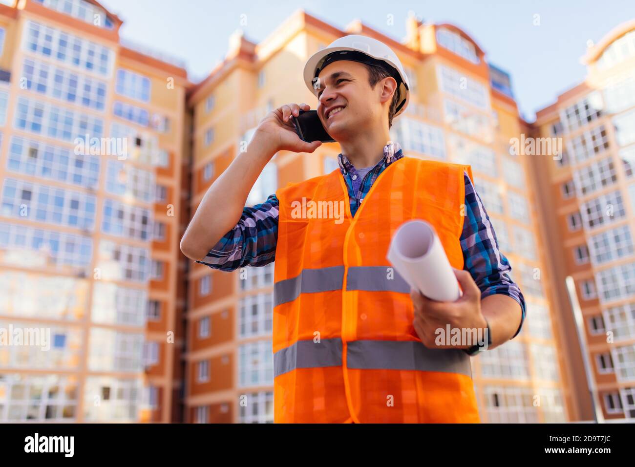Engineer with plan in his hand talking on cell phone on construction ...