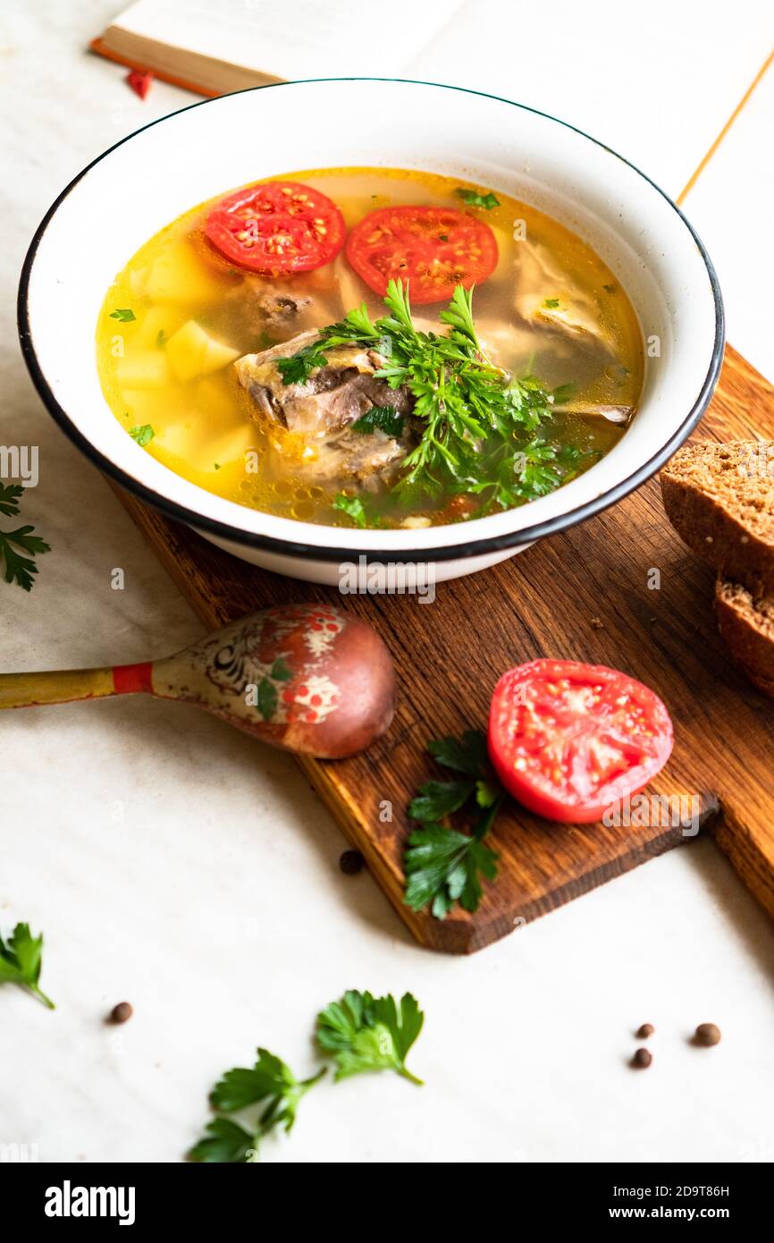 fish soup with carp, potatoes, parsley, tomato in enamel bowl stands on ...