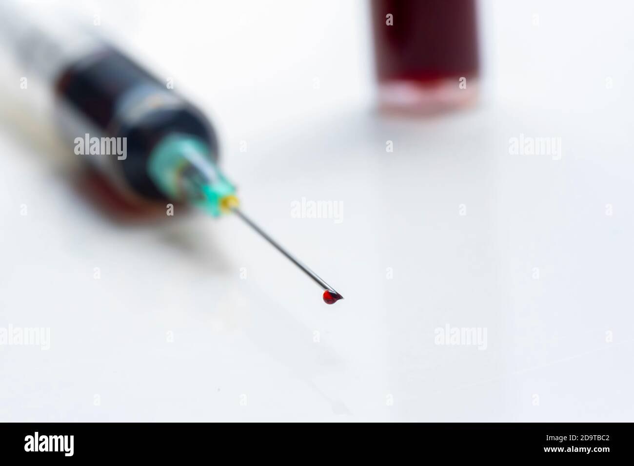 drop of blood on the tip of a syringe needle with an unfocused blood ...