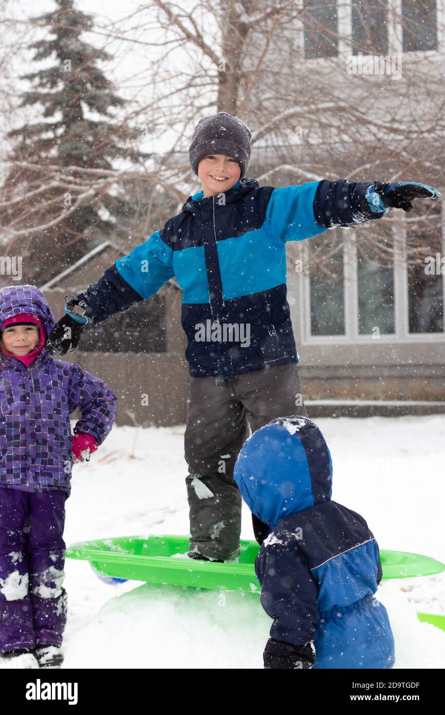 Child standing on sled in snow smiling and looking at camera while ...