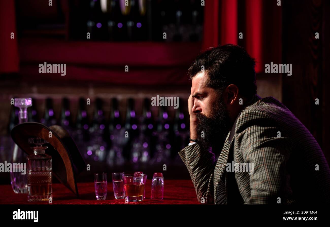Handsome bearded man looking tired and upset drinking whiskey alone at ...