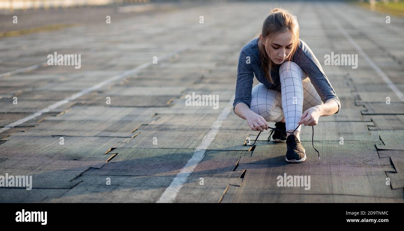 Female runner lacing her sneakers on a stadium running track. Healthy ...