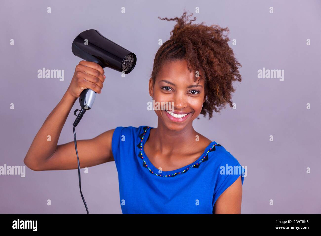 Young African American woman using an hair dryer on her afro hair ...