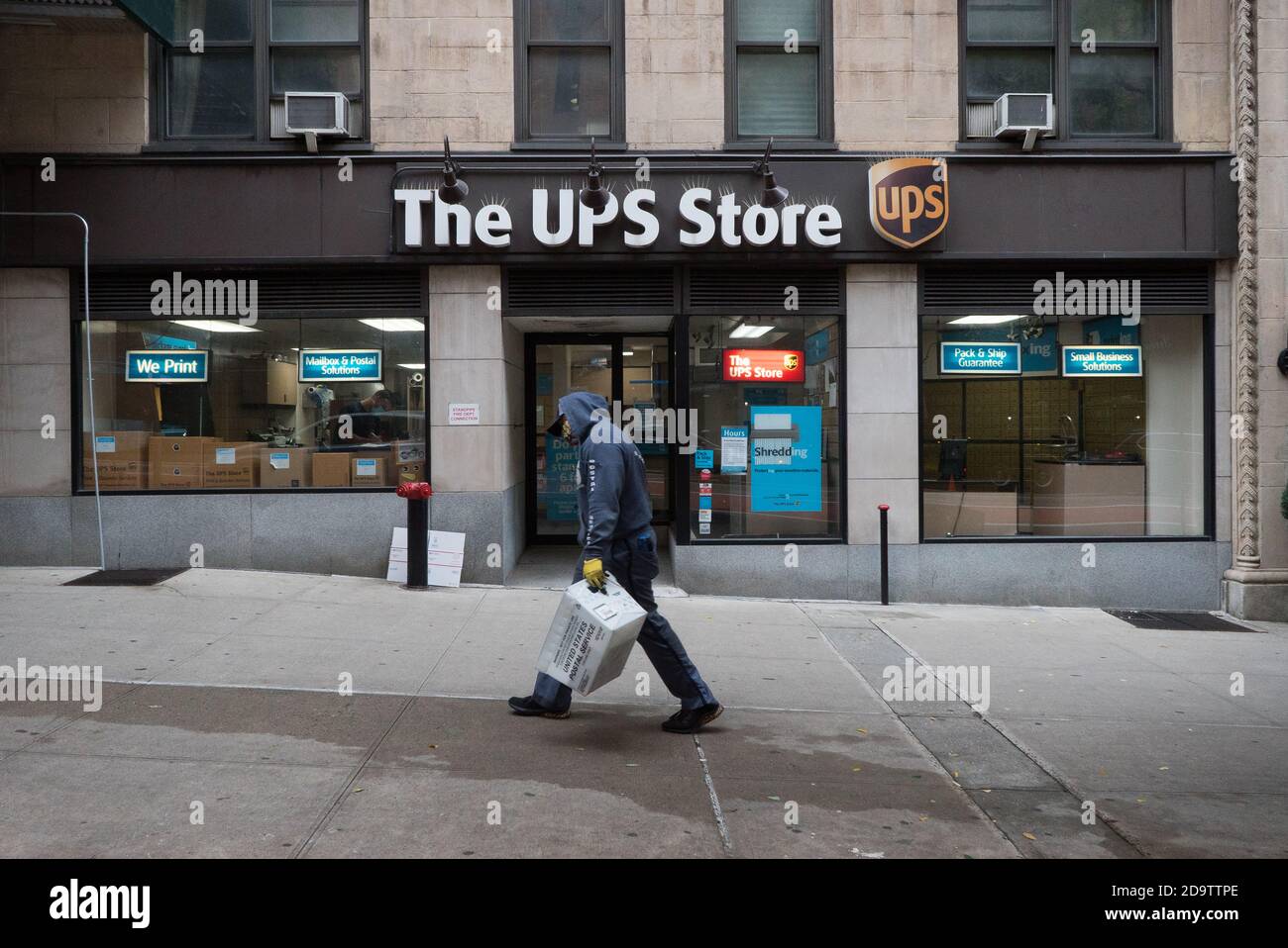 A USPS mailman wearing a mask walks in front of a UPS store in midtown ...