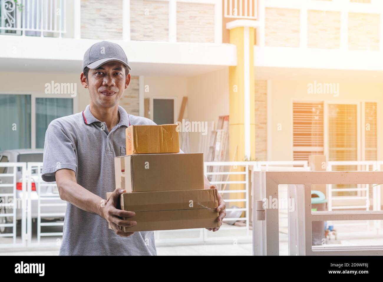 Deliverers in gray uniform stand holding boxes and smiling at customer ...