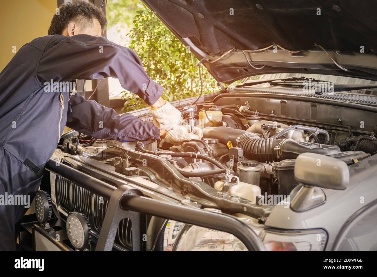 Car repairman wearing a dark blue uniform was wrenching at the engine ...