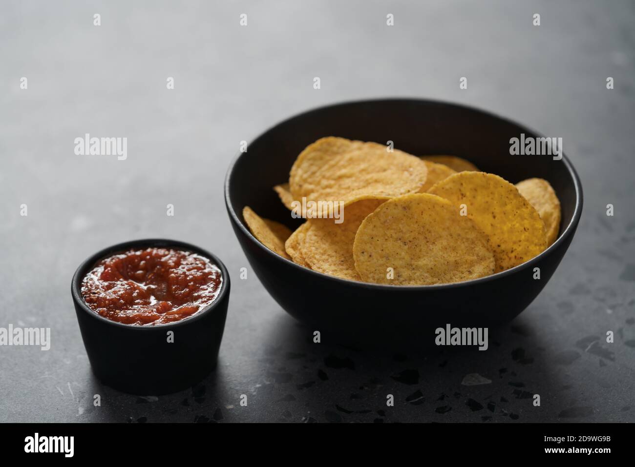 Round nachos in black ceramic bowl on concrete background with red ...