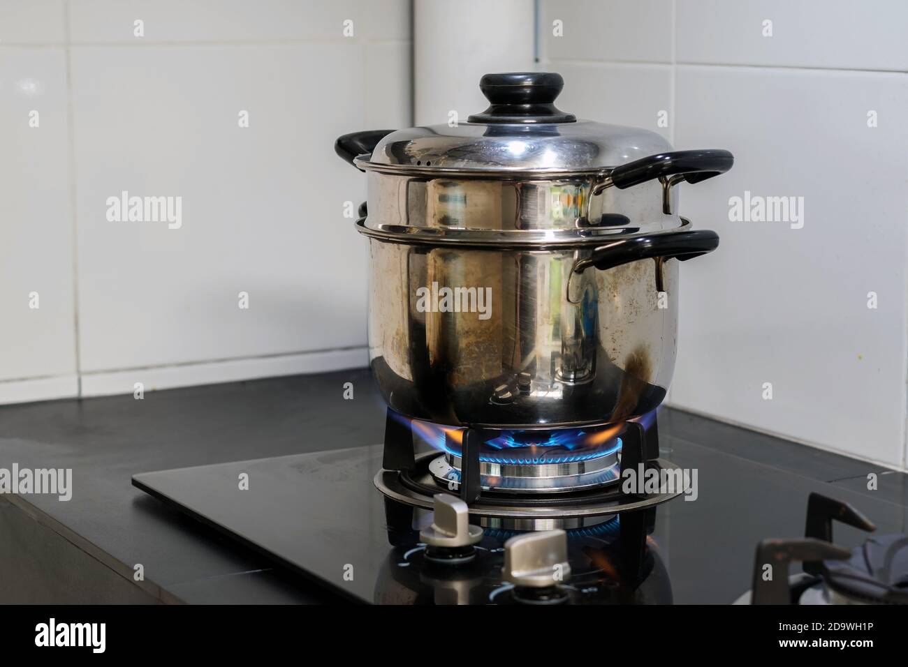 A stainless steel pot is placed on a gas stove that is turned on for ...