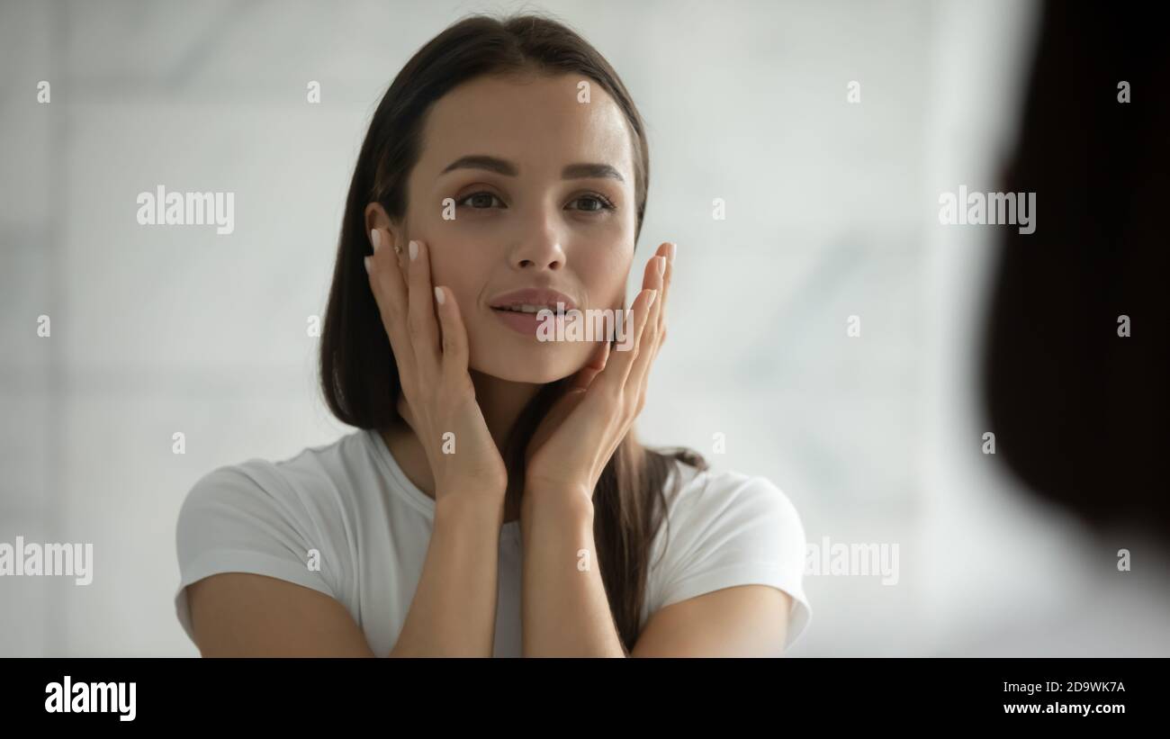 Mirror reflection of pretty young female visually checking skin health ...