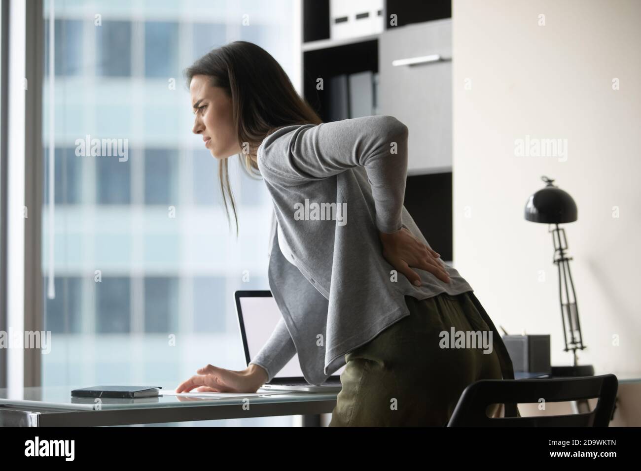 Suffering woman employee leaning forward holding hand on lower back ...