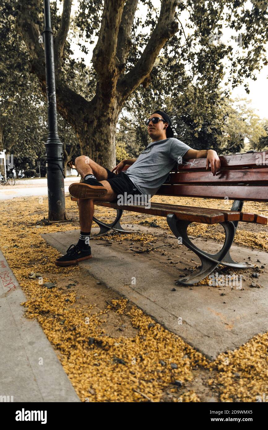 Vertical shot of a cool young man sitting on a bench in a park Stock ...