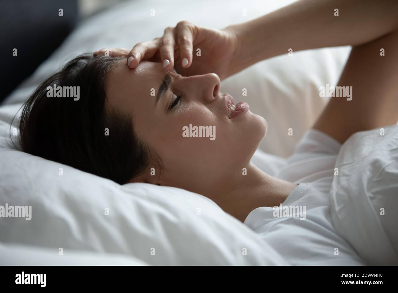 Sad female lying in pillows touching forehead suffering from migraine ...
