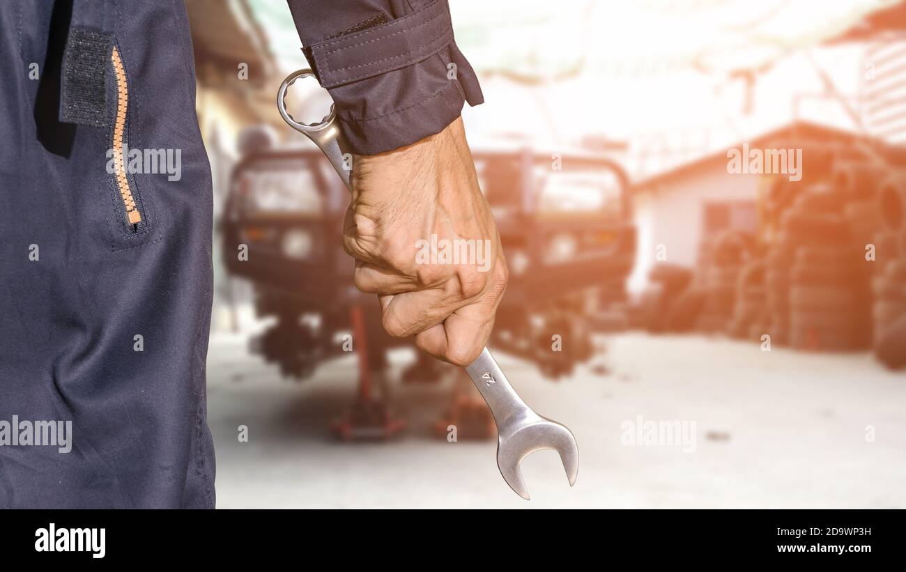 Car repairman wearing a dark blue uniform standing and holding a wrench ...