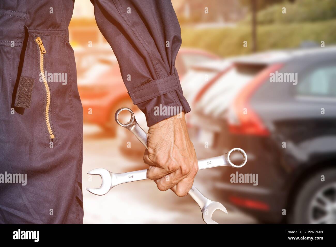 Car repairman wearing a dark blue uniform standing and holding a wrench ...