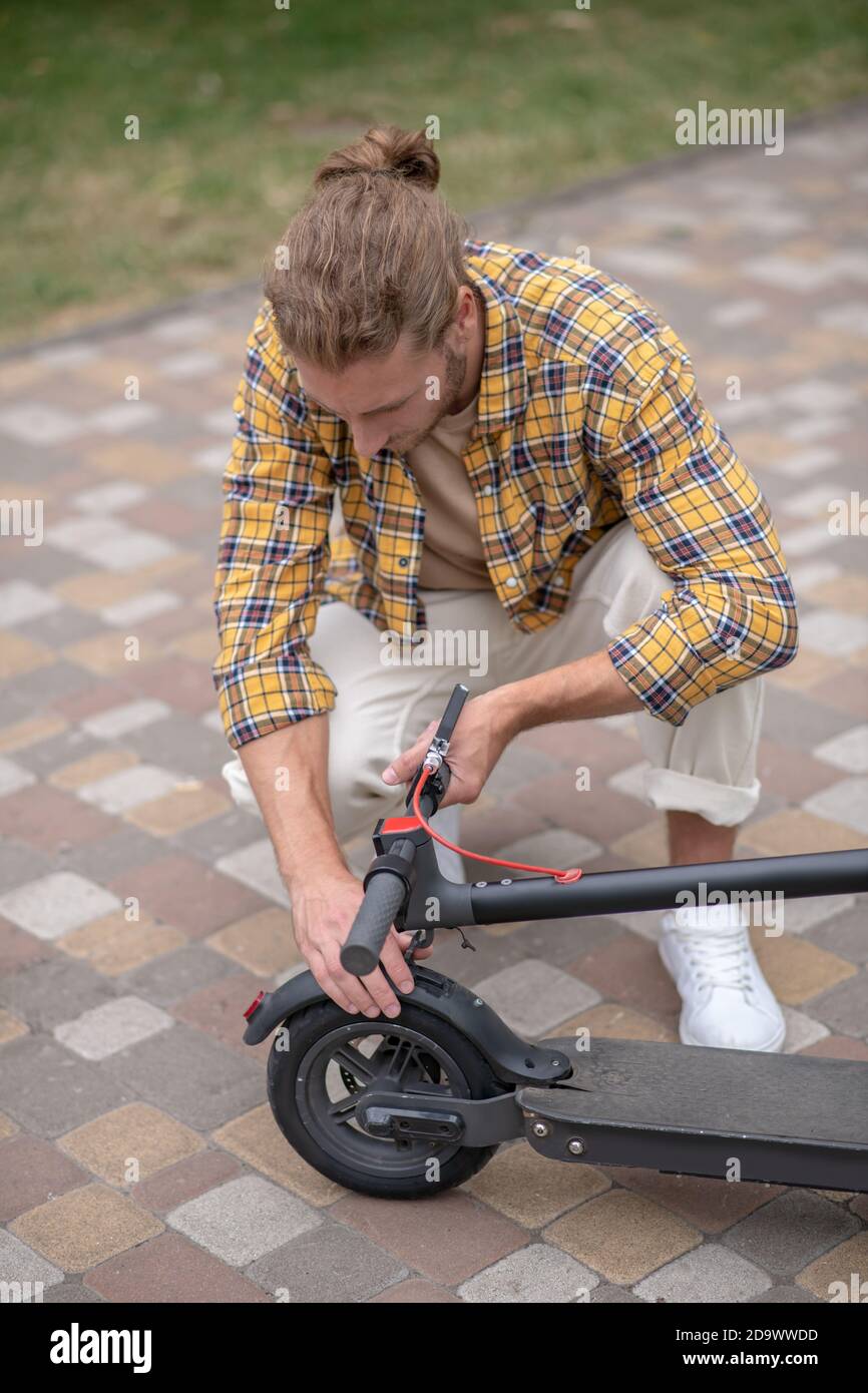 Electric vehicle. Man sitting on his hunkers and regulating his scooter ...