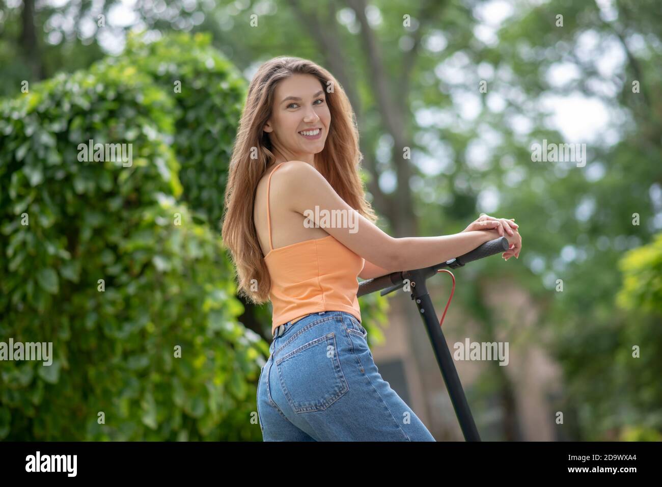 Leisure. Long-haired young girl riding a scooter in the park and ...