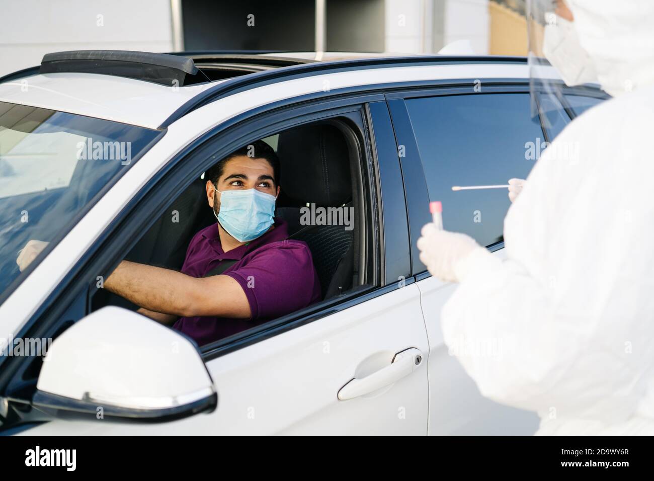 Doctor doing a PCR test COVID-19 on a patient through the car window ...