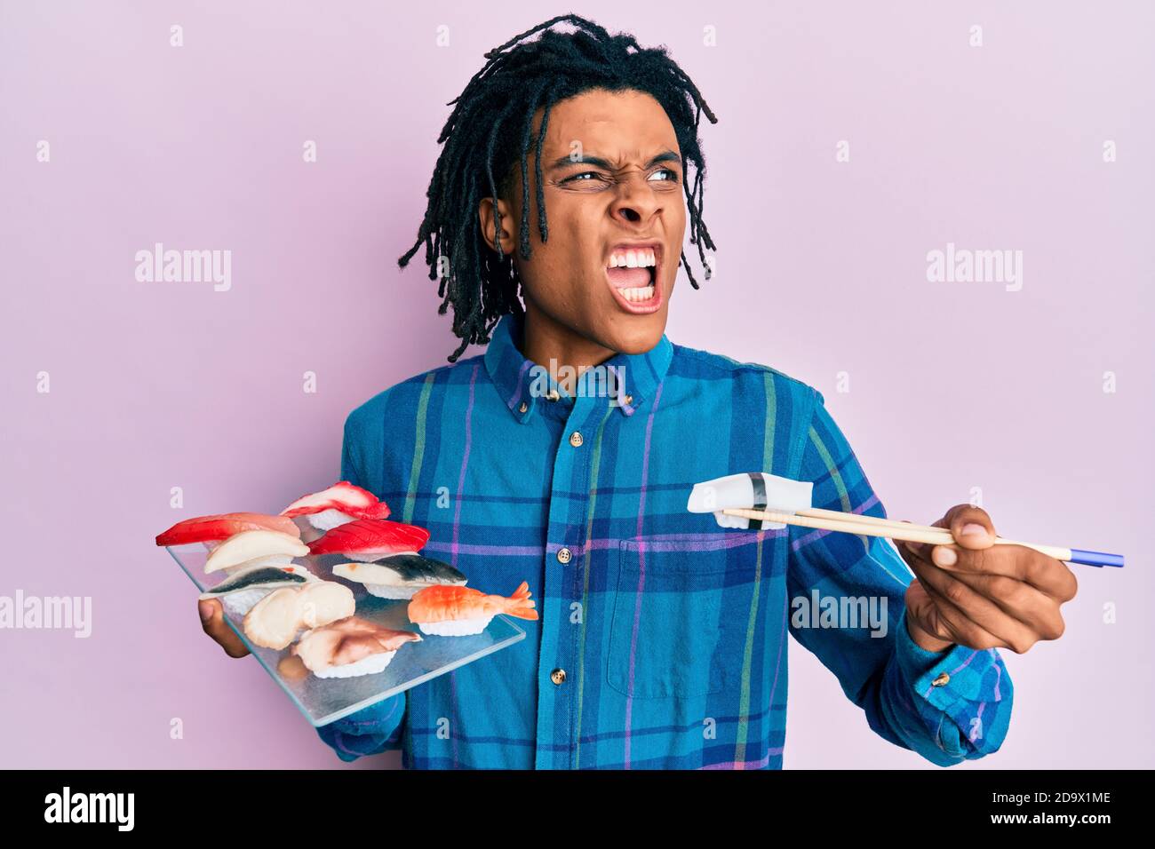 Young african american man eating sushi using chopsticks angry and mad ...