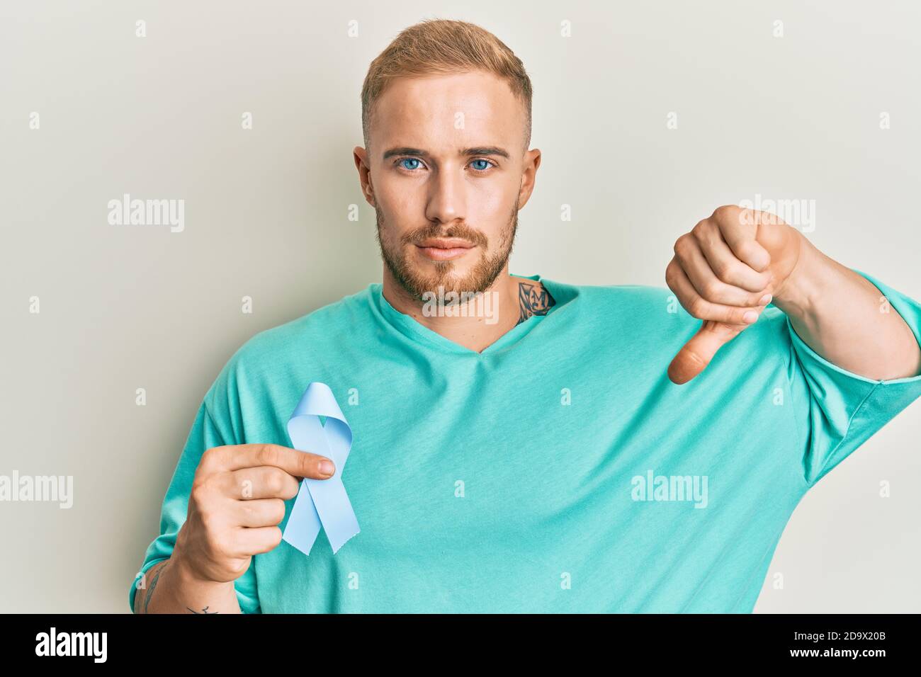 Young caucasian man holding blue ribbon with angry face, negative sign ...