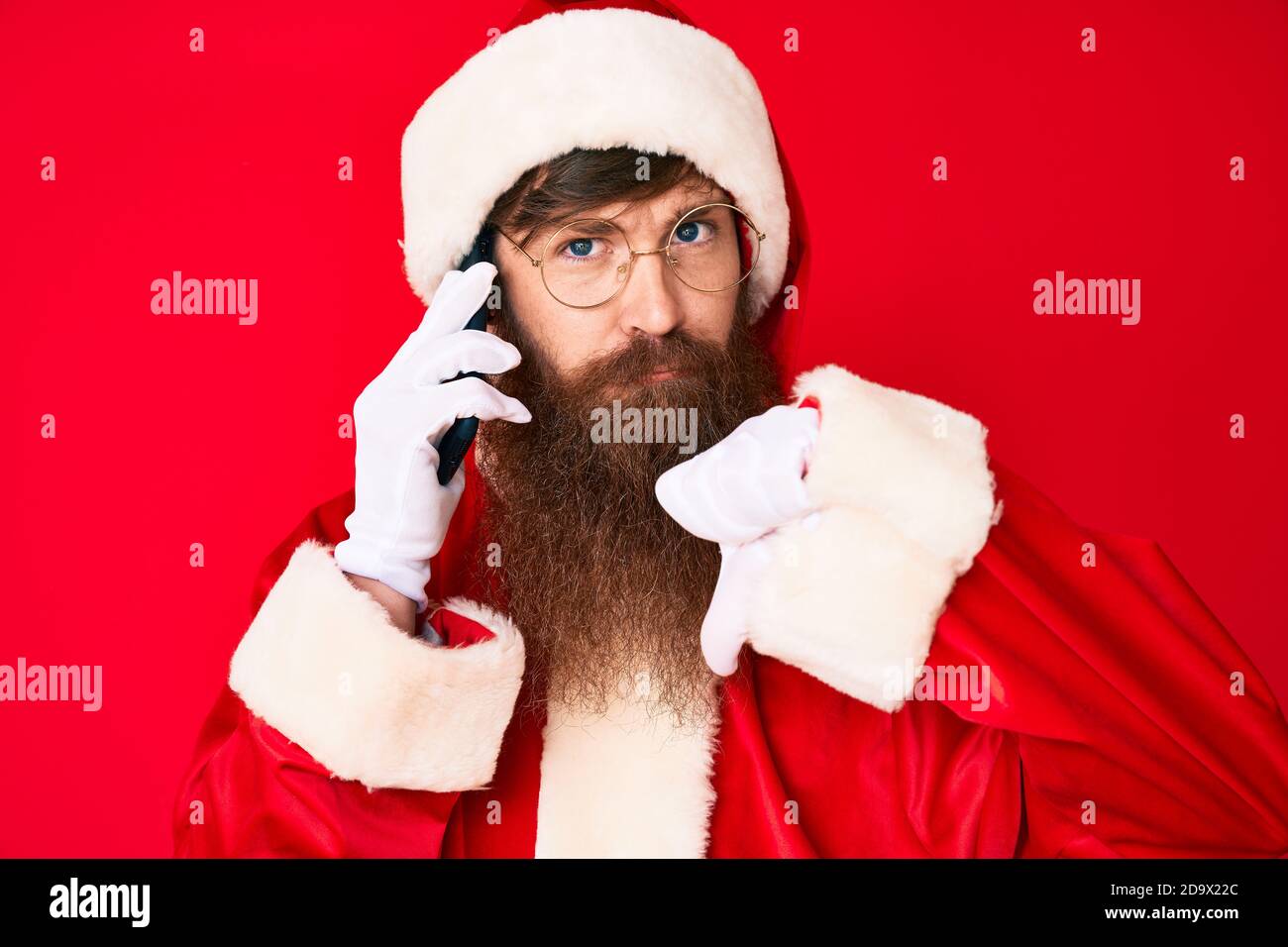 Handsome young red head man with long beard wearing santa claus costume ...
