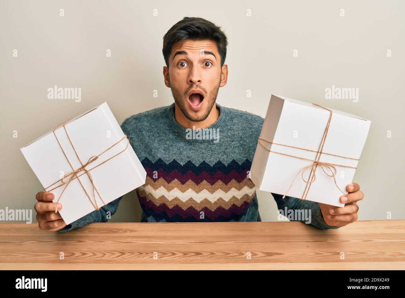 Young handsome man holding gifts afraid and shocked with surprise and ...