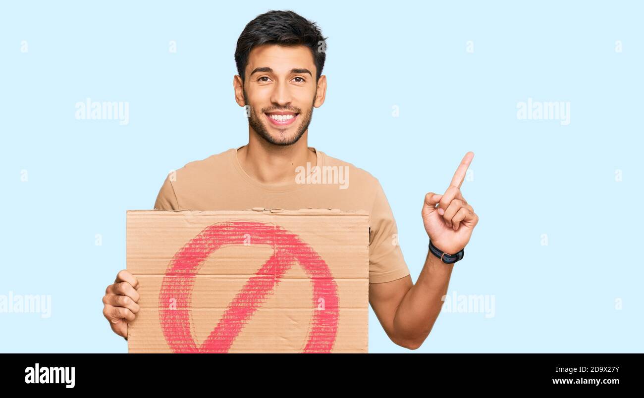 Young handsome man holding prohibited warning banner surprised with an ...