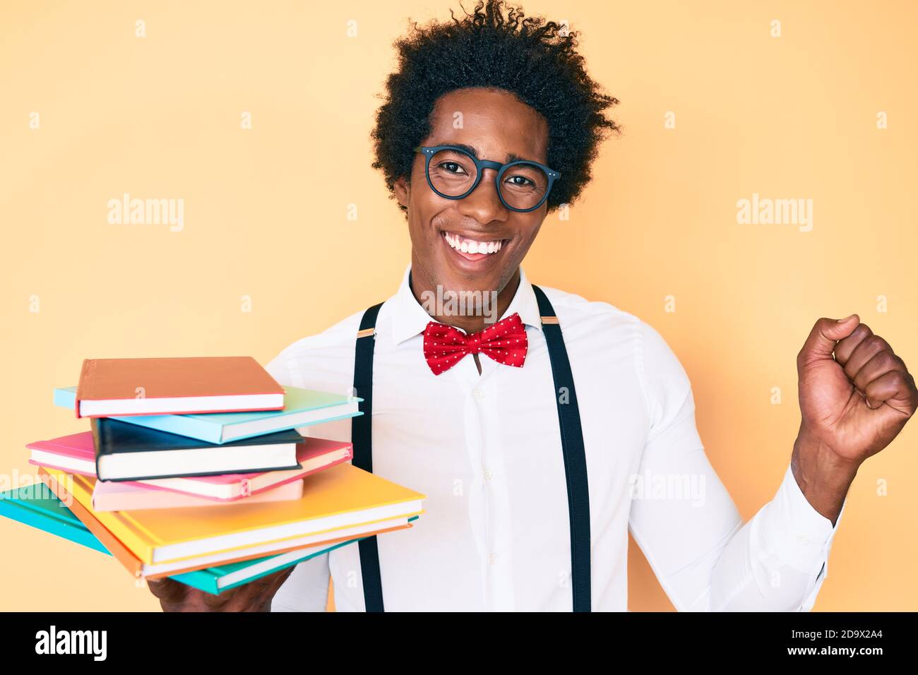 Handsome african american nerd man with afro hair holding books screaming proud, celebrating ...