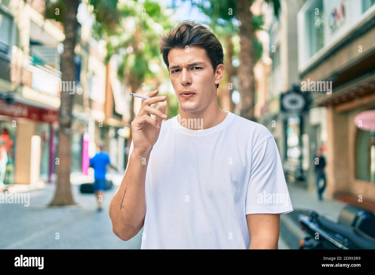 Young caucasian man with serious expression smoking cigarette at the ...