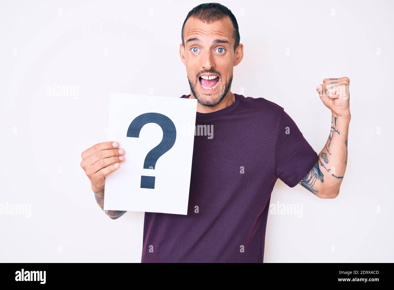 Young handsome man with tattoo holding question mark screaming proud ...