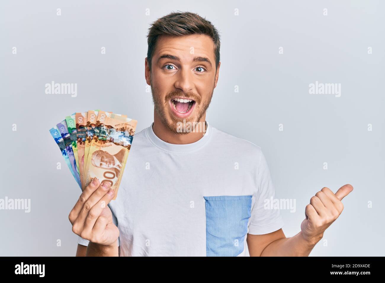 Handsome caucasian man holding canadian dollars pointing thumb up to ...
