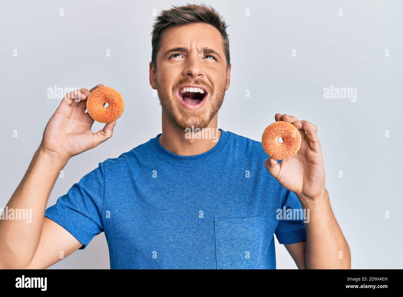 Handsome caucasian man eating donuts angry and mad screaming frustrated ...