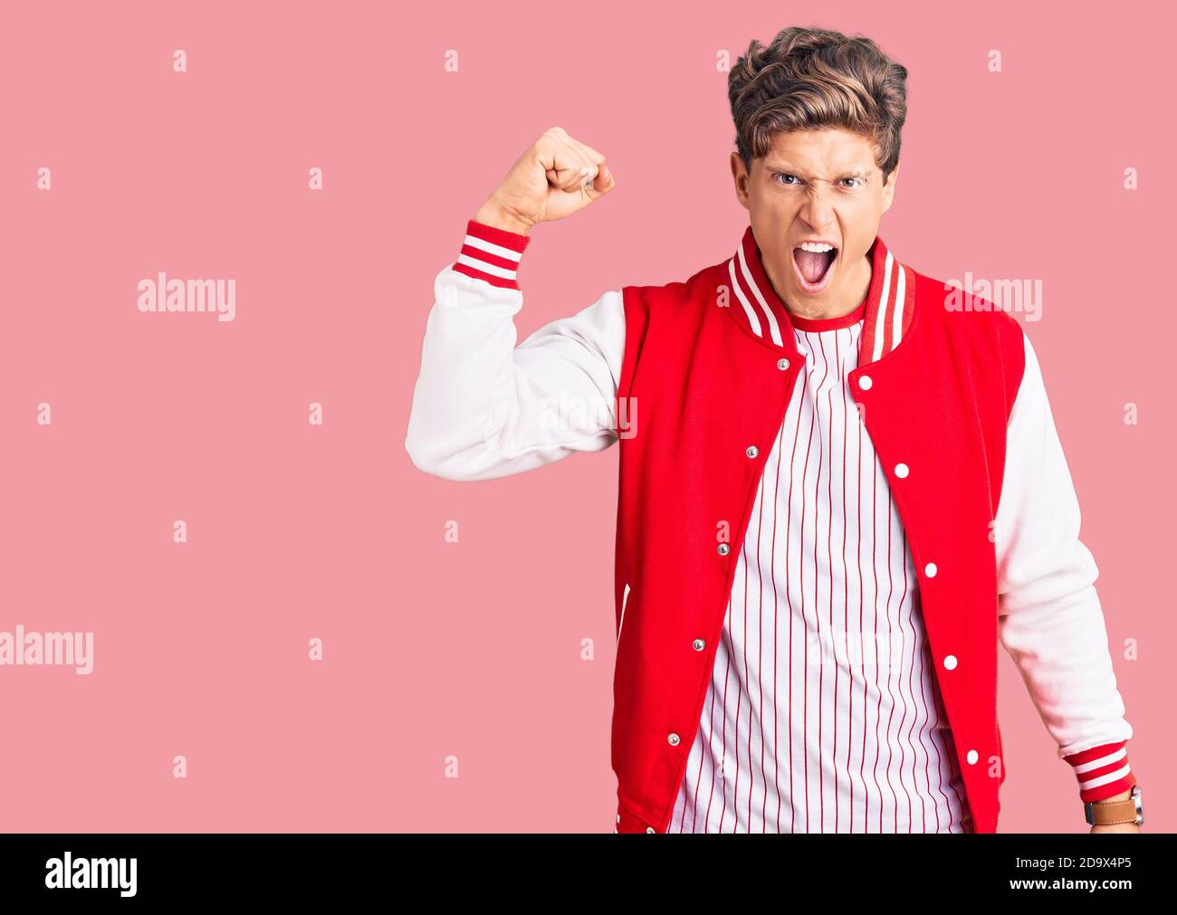 Young handsome man wearing baseball uniform angry and mad raising fist ...