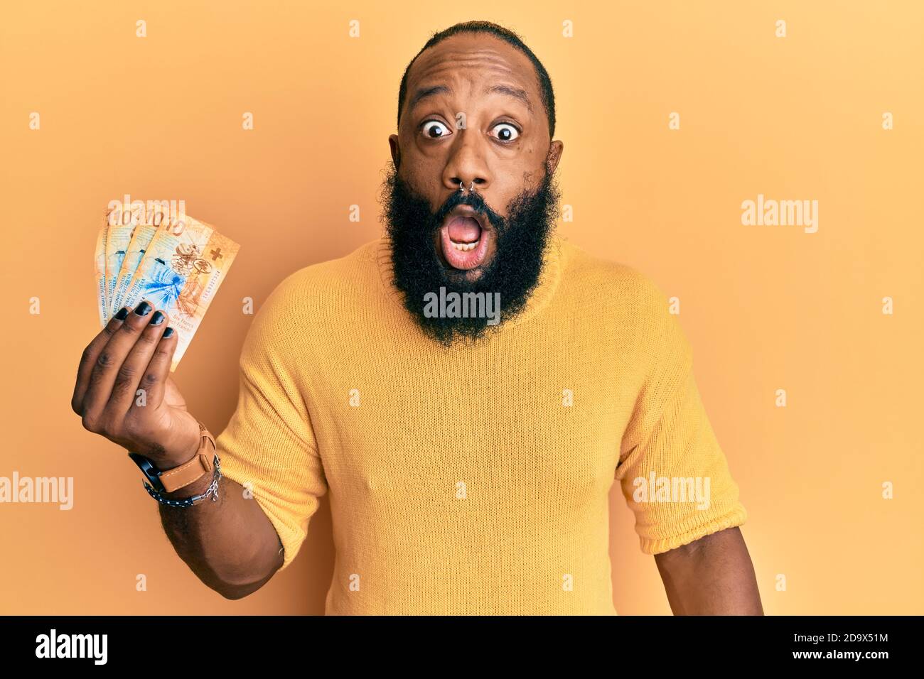 Young african american man holding 10 swiss franc banknotes scared and ...