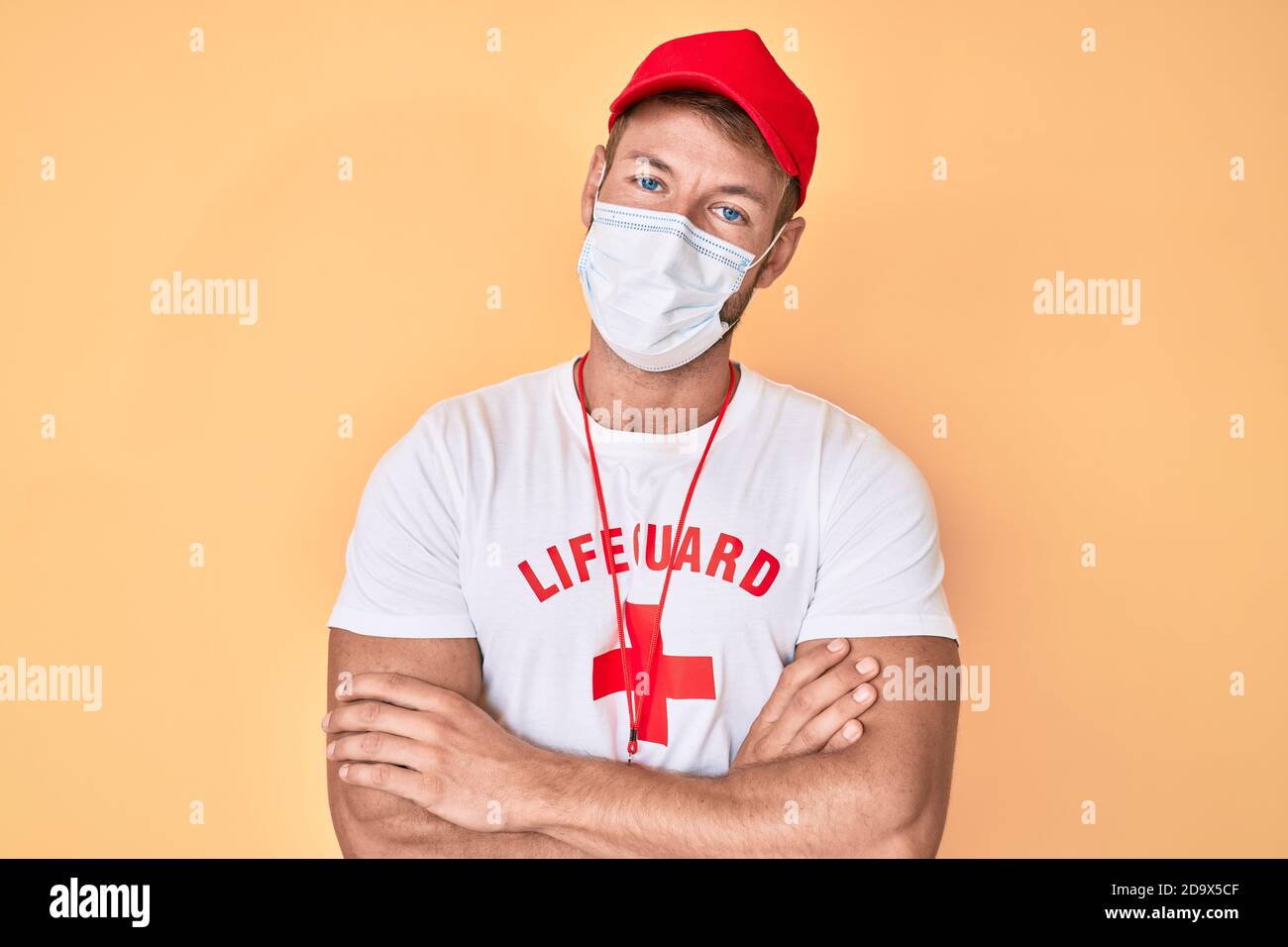 Young caucasian man wearing lifeguard t shirt using medical mask happy ...