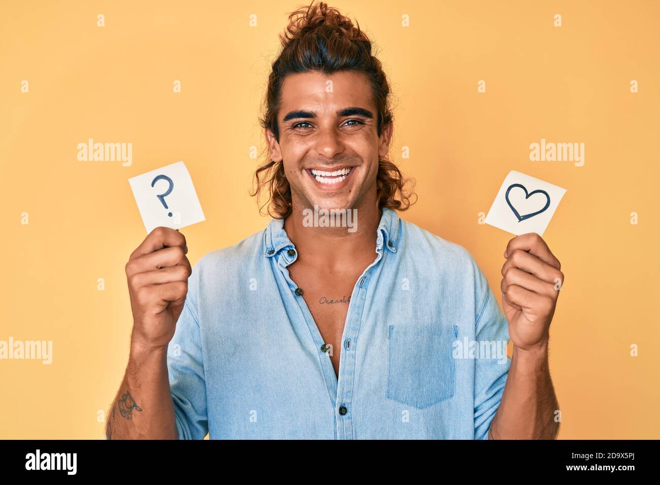 Young hispanic man holding heart and question mark reminder smiling ...