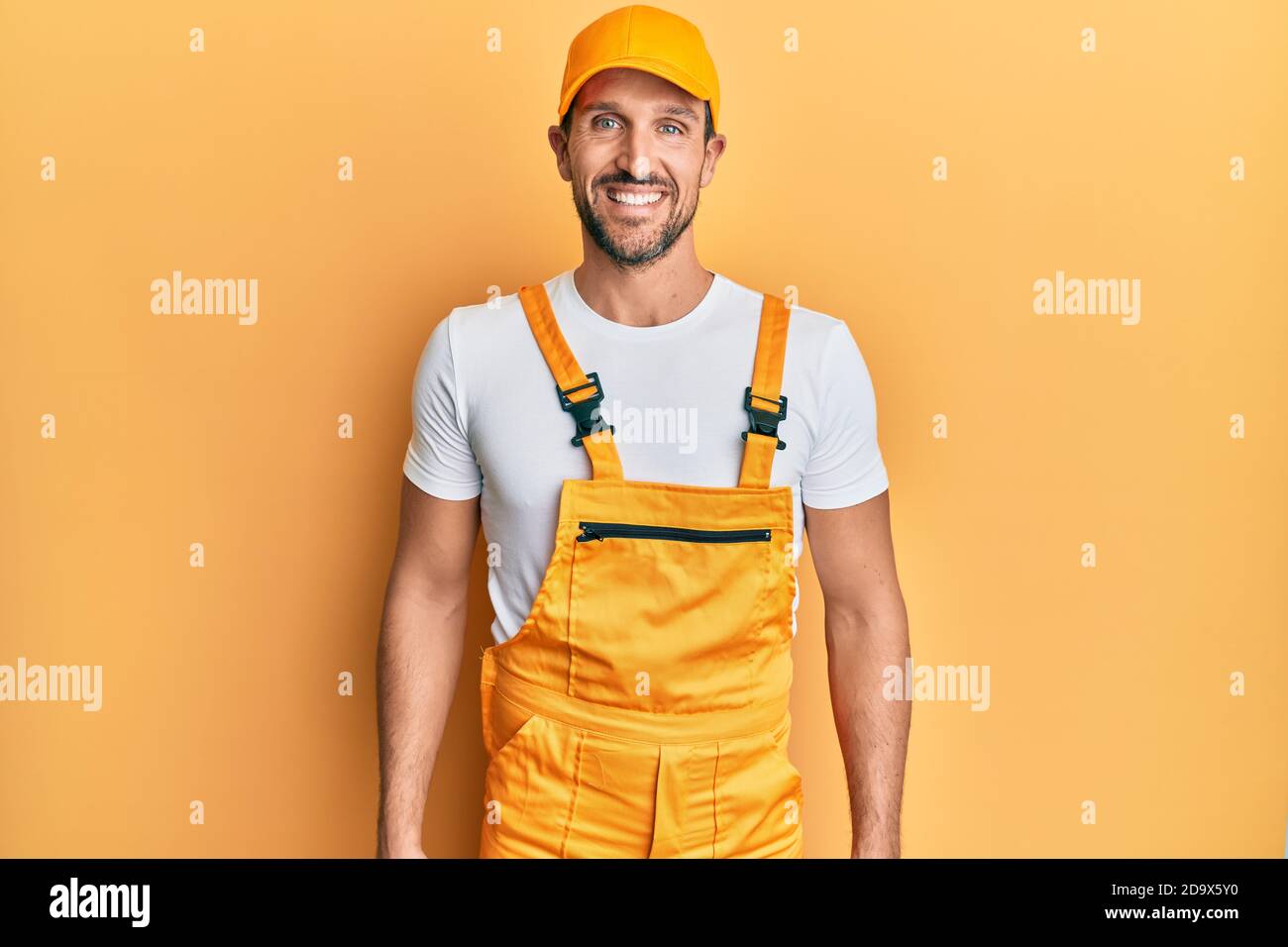 Young handsome man wearing handyman uniform over yellow background with ...