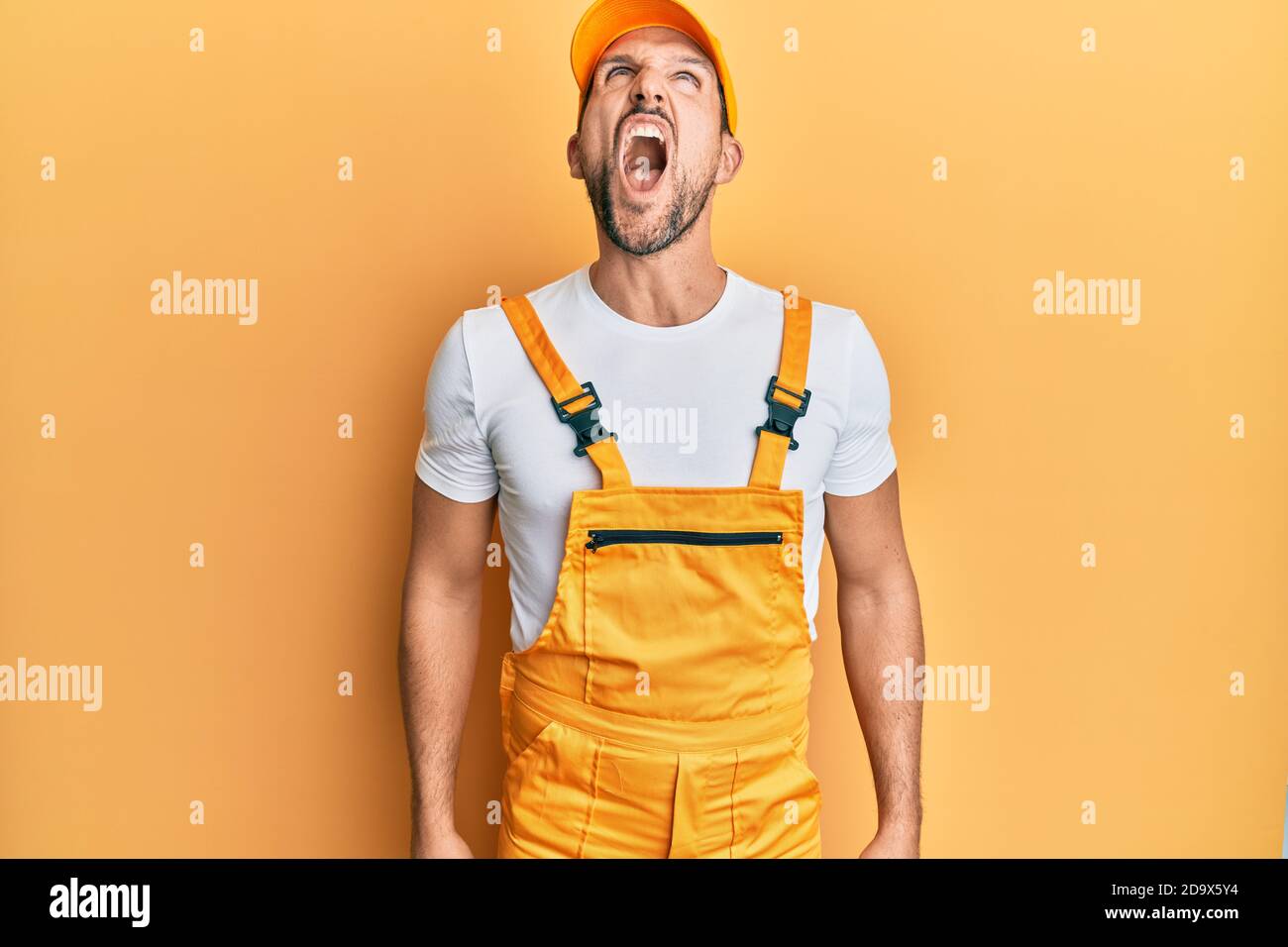 Young handsome man wearing handyman uniform over yellow background ...
