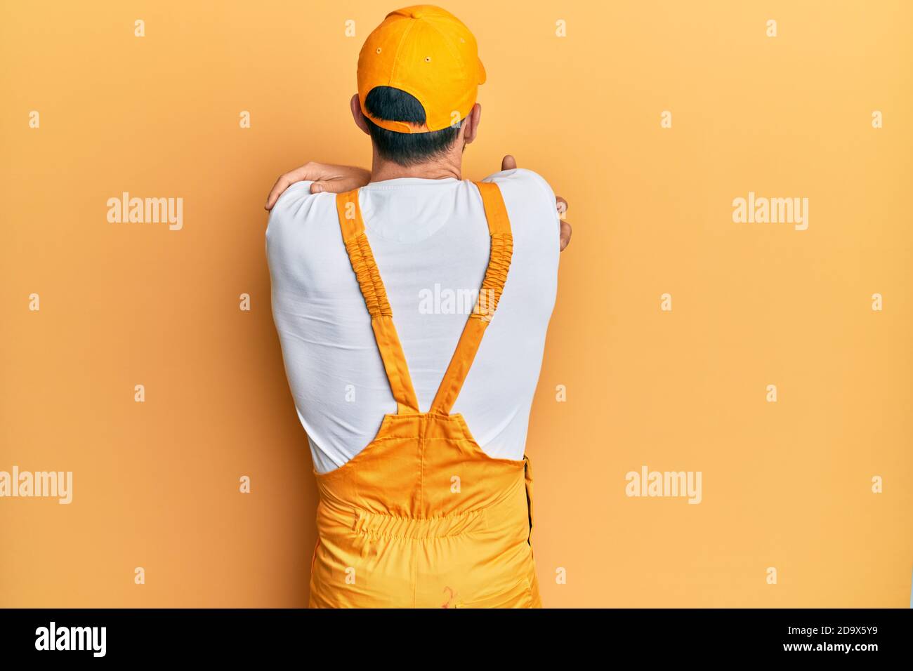 Young handsome man wearing handyman uniform over yellow background ...
