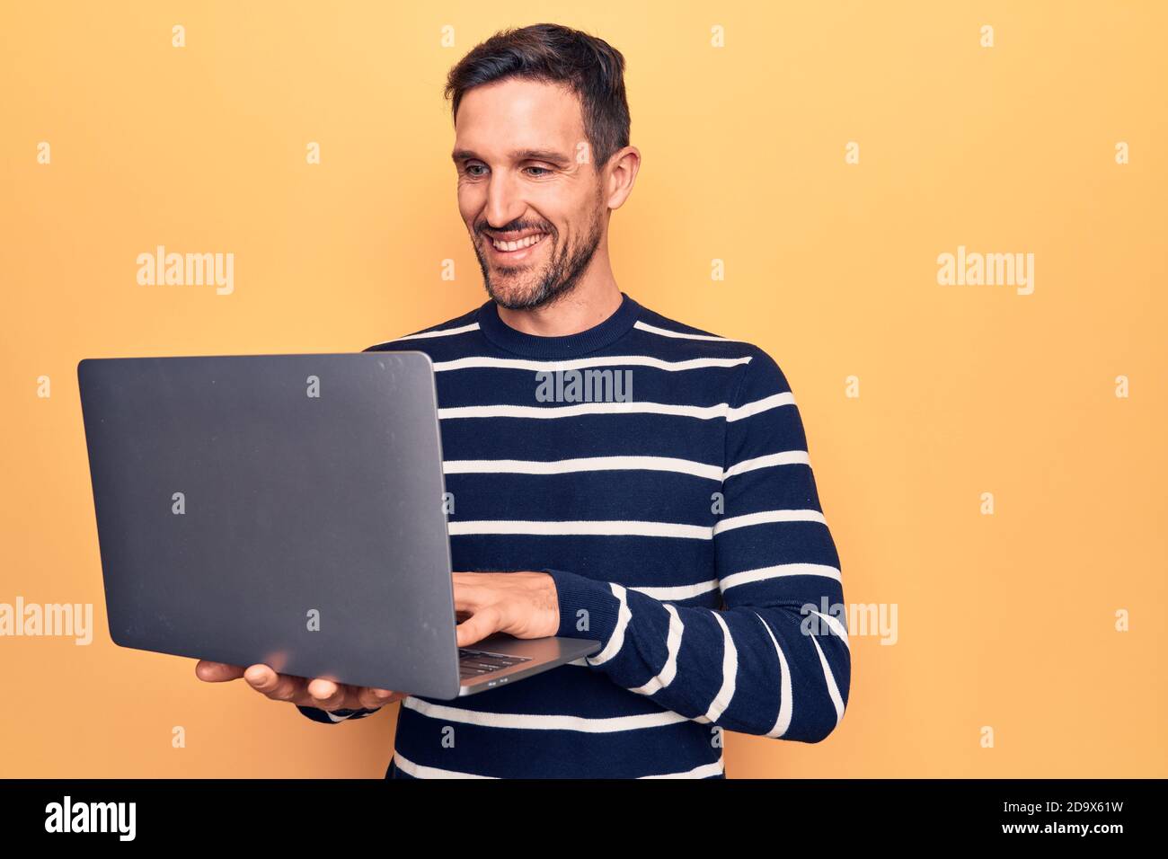 Young handsome man working using laptop standing over isolated yellow ...