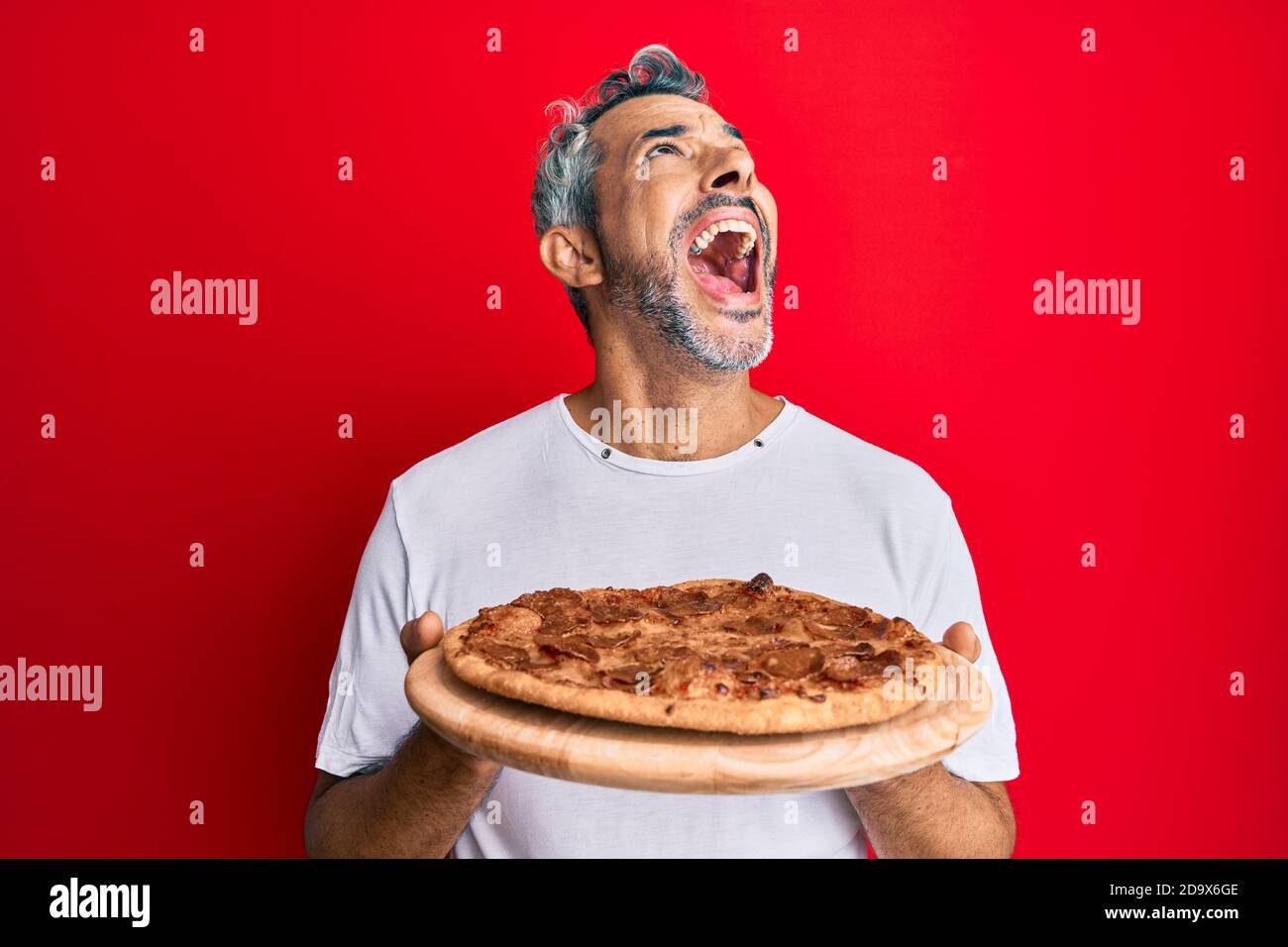 Middle age grey-haired man holding italian pizza angry and mad ...