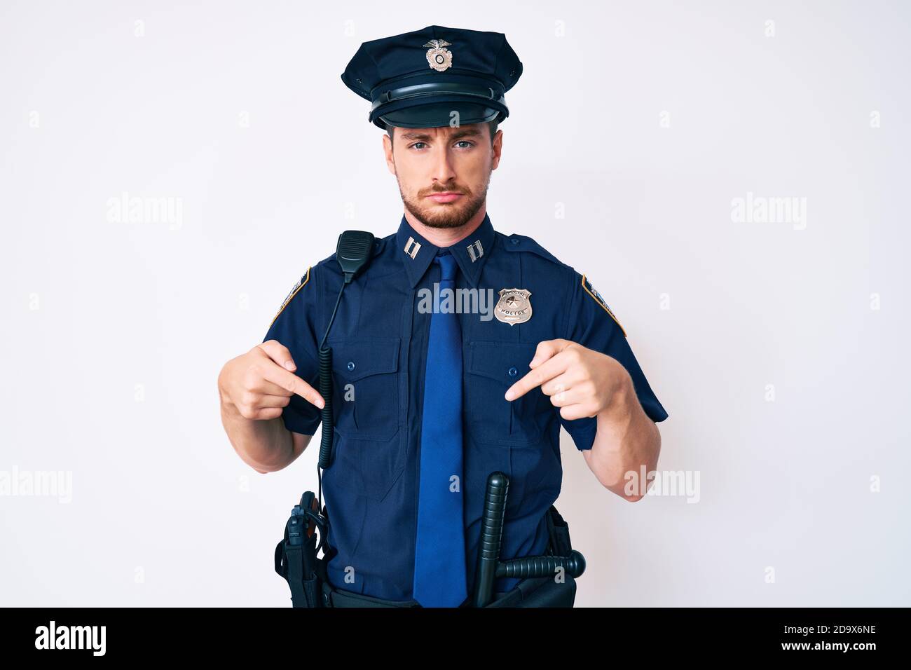 Young caucasian man wearing police uniform pointing down looking sad ...